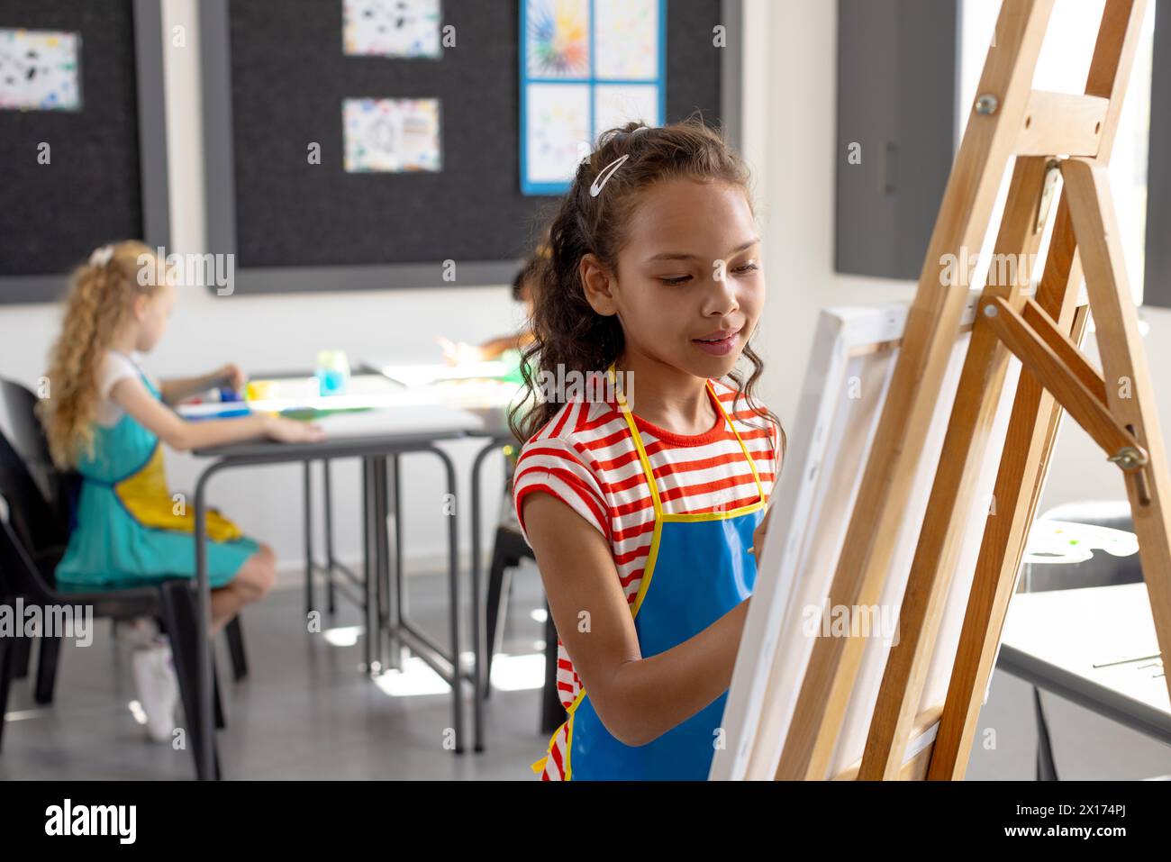 In school, during art class, a young biracial girl wearing a striped ...