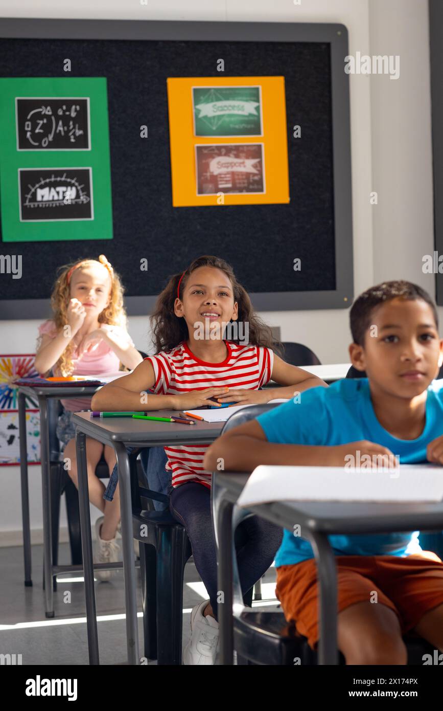 In school, diverse group of young students sitting at desks in the ...