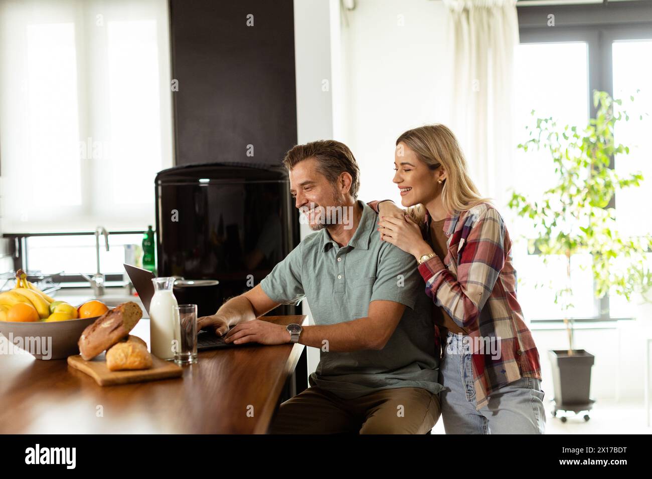 A cheerful couple enjoys a light-hearted moment in their sunny kitchen ...