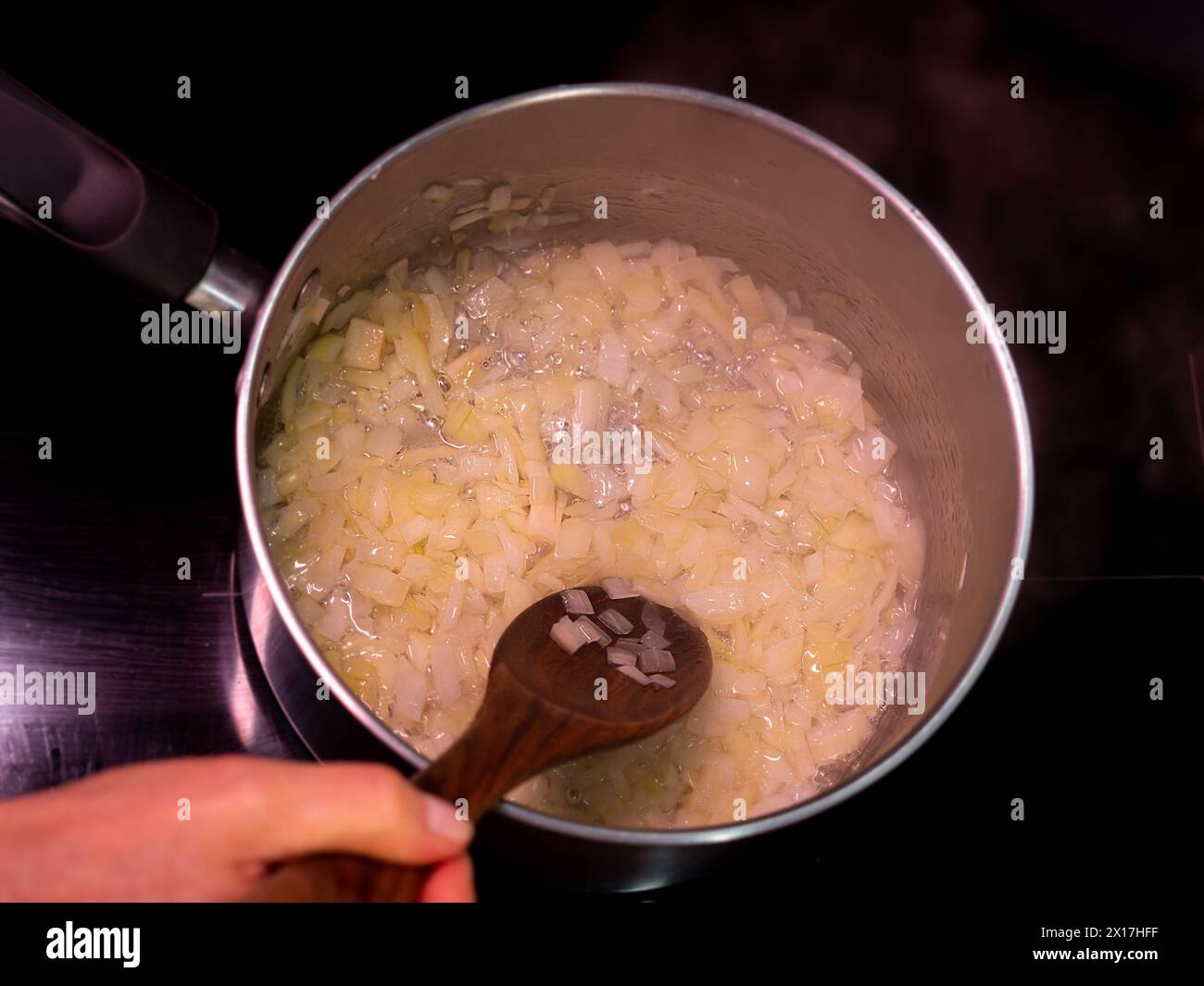 cooking diced onion pot frying in oil, silver pot black background ...