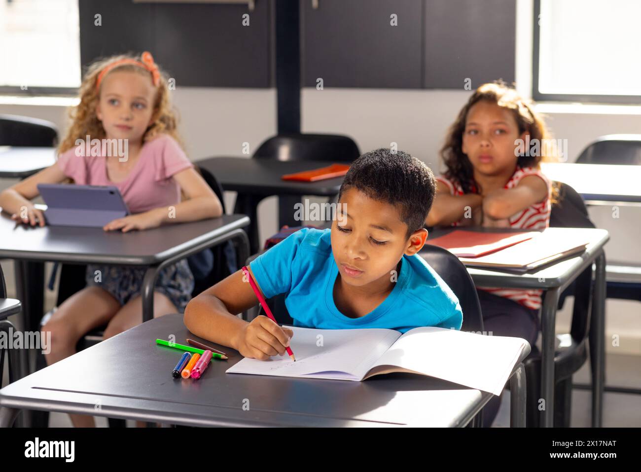 In school, in classroom, boy in blue shirt writing in notebook, two ...