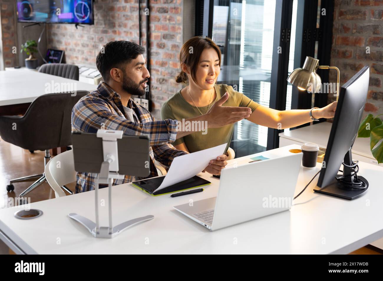 Senior Asian woman points at screen, young colleague watches in a ...