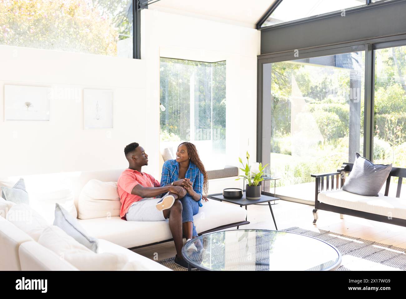 African American couple sitting on white sofa, holding hands and ...