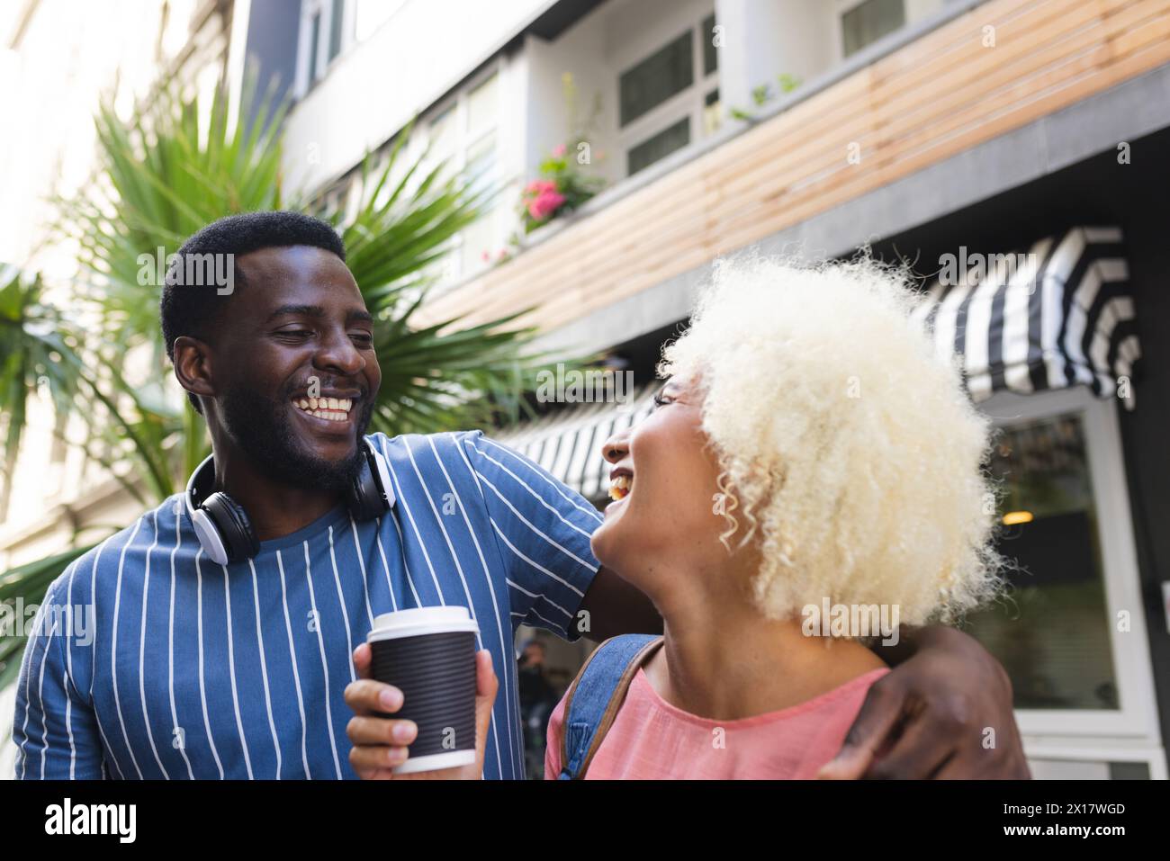 Diverse couple laughing, holding coffee outside cafe Stock Photo - Alamy
