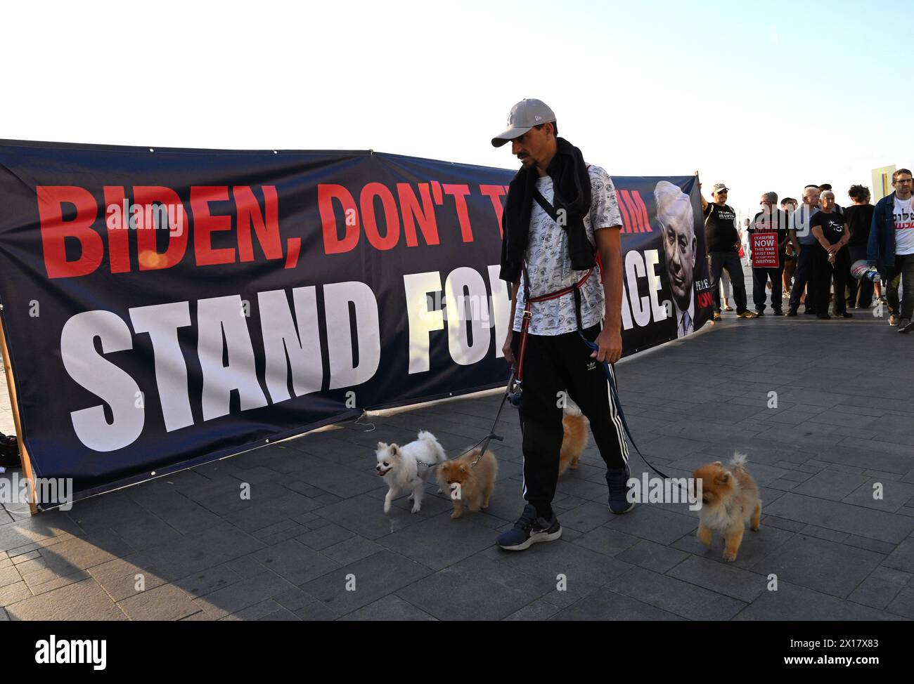 Tel Aviv, Israel. 15th Apr, 2024. A man walks dogs past a banner with a ...