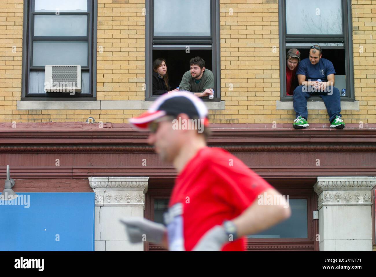 People hang out of their apartment windows as they watch runners in the ...
