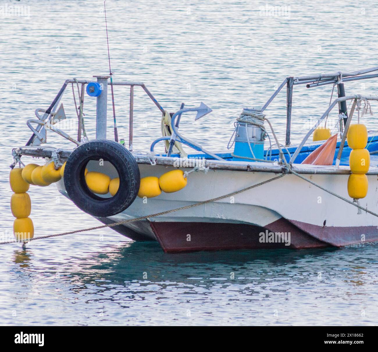 Moored fishing boat with yellow buoys and a tire on calm blue sea ...
