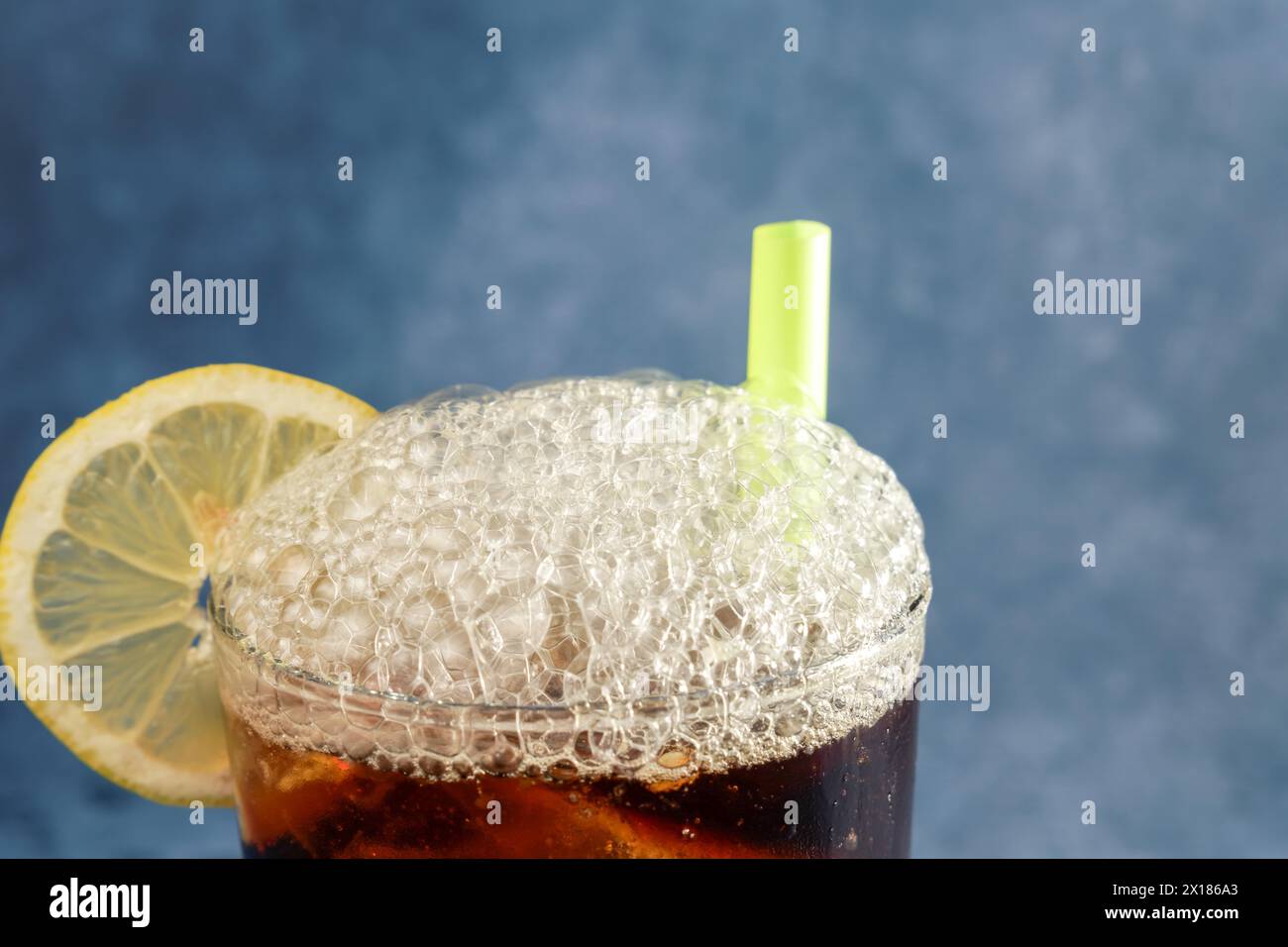 Cola with ice and lemon with foam spilling out of the crystal glass ...