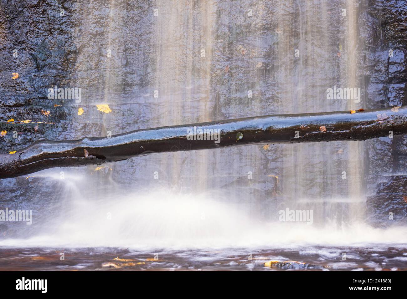 Tree log by a waterfall with falling water by a rock face Stock Photo ...