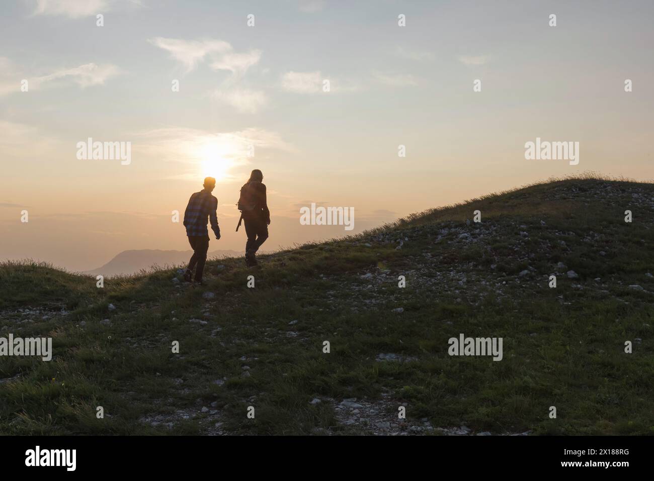 Female hiker silhouette with a backpack walking and following the trail uphill, enjoying the sky ...