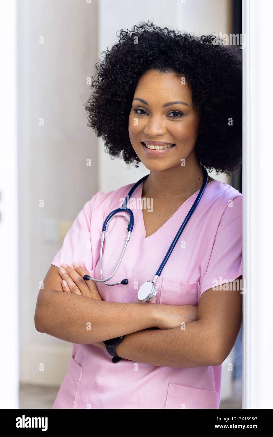 Biracial nurse standing at home, arms crossed, wearing pink scrubs ...