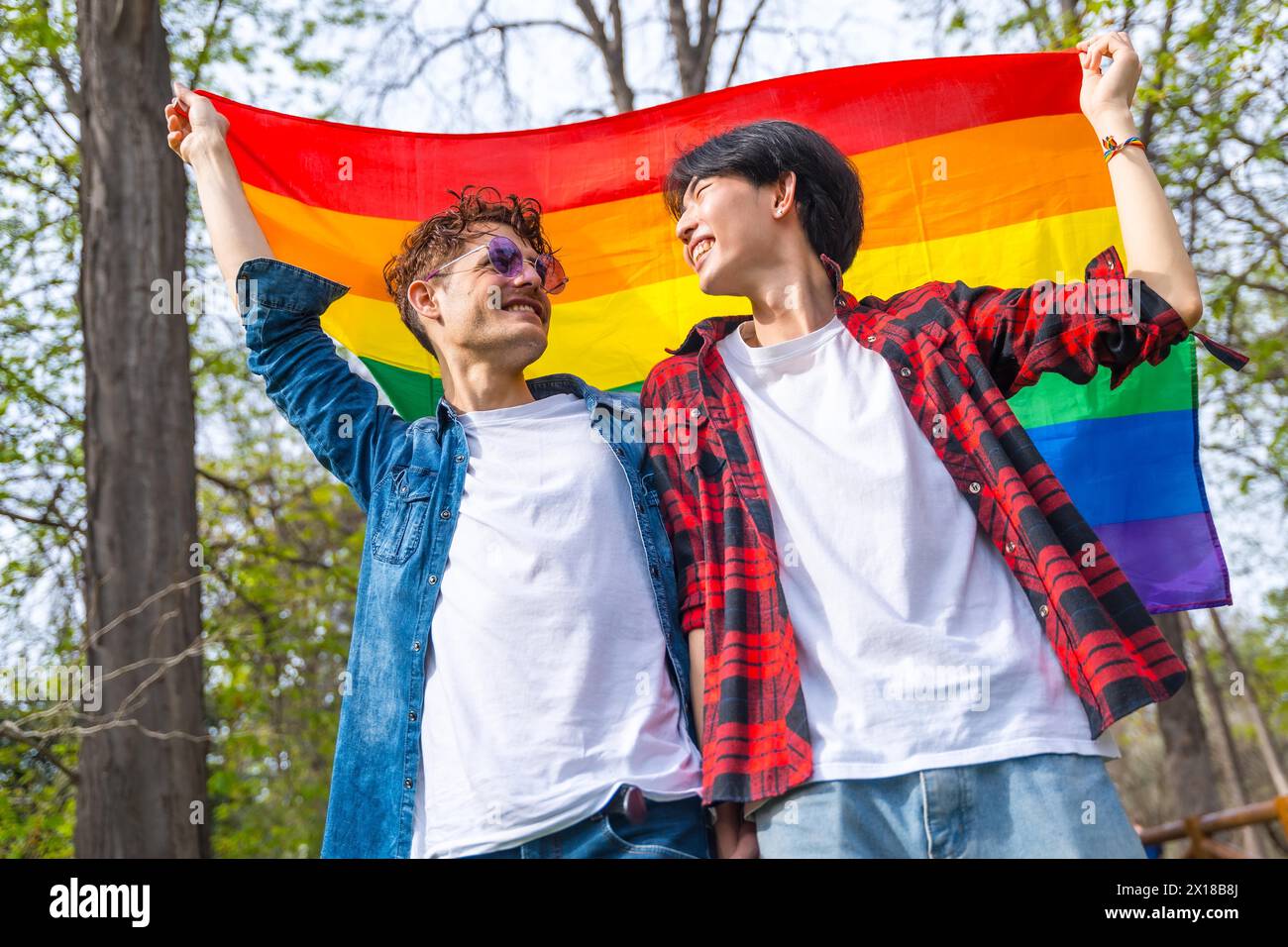 Low angle view photo of a gay couple looking at each other smiling and ...