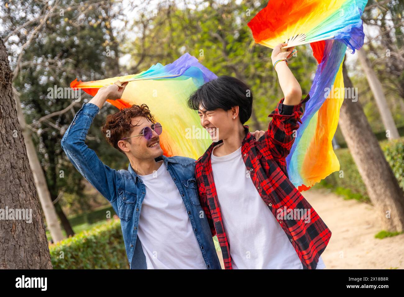 Multiracial gay couple raising lgbt rainbow hand fan smiling walking in ...