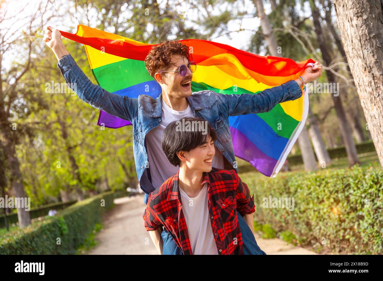 Multiracial gay couple waving lgbt flag piggybacking celebrating ...