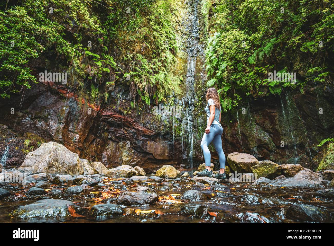 Description: Female tourist enjoys a green overgrown waterfall. 25 ...