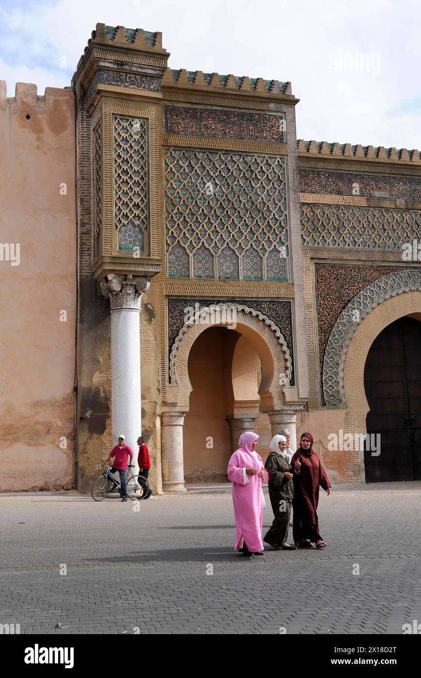 Meknes, People in traditional dress walk past a decorated gate with ...