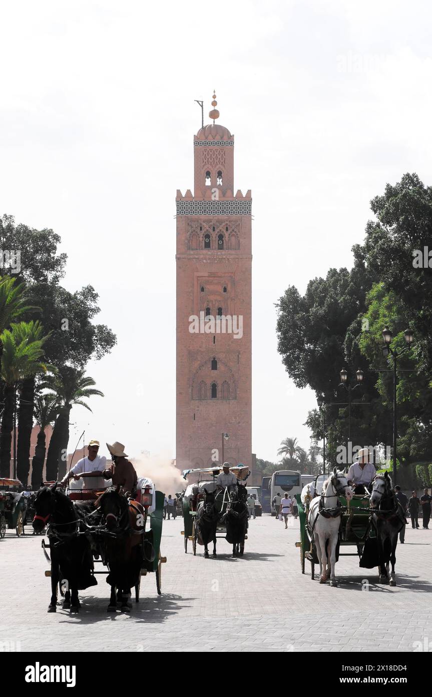 Marrakech, A historic minaret towering over a square with horse-drawn ...