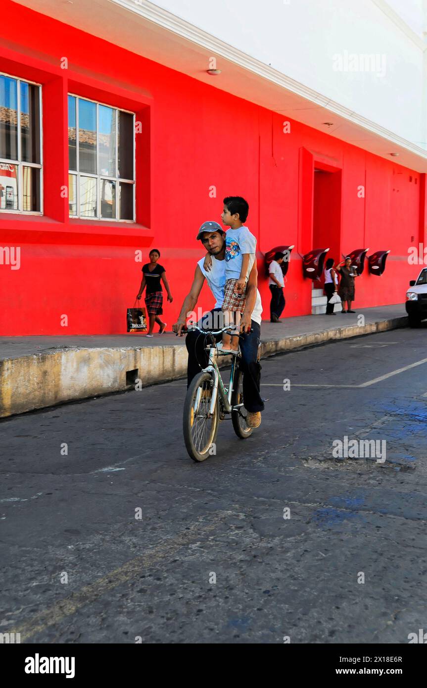 Leon, Nicaragua, A man and a boy ride together on a bicycle past a red ...