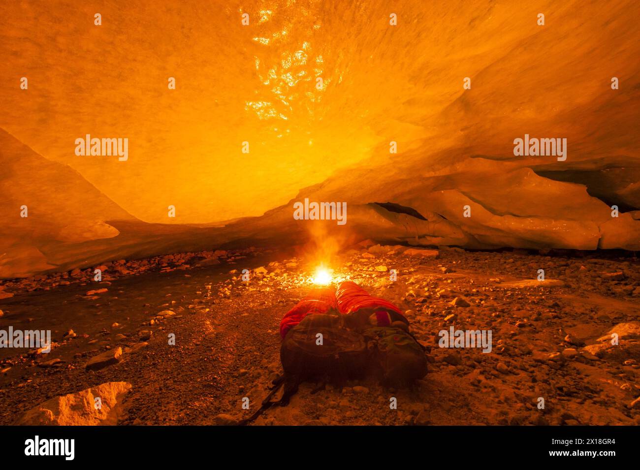 A glowing fire in a cave with a sleeping bag lying next to it creates ...