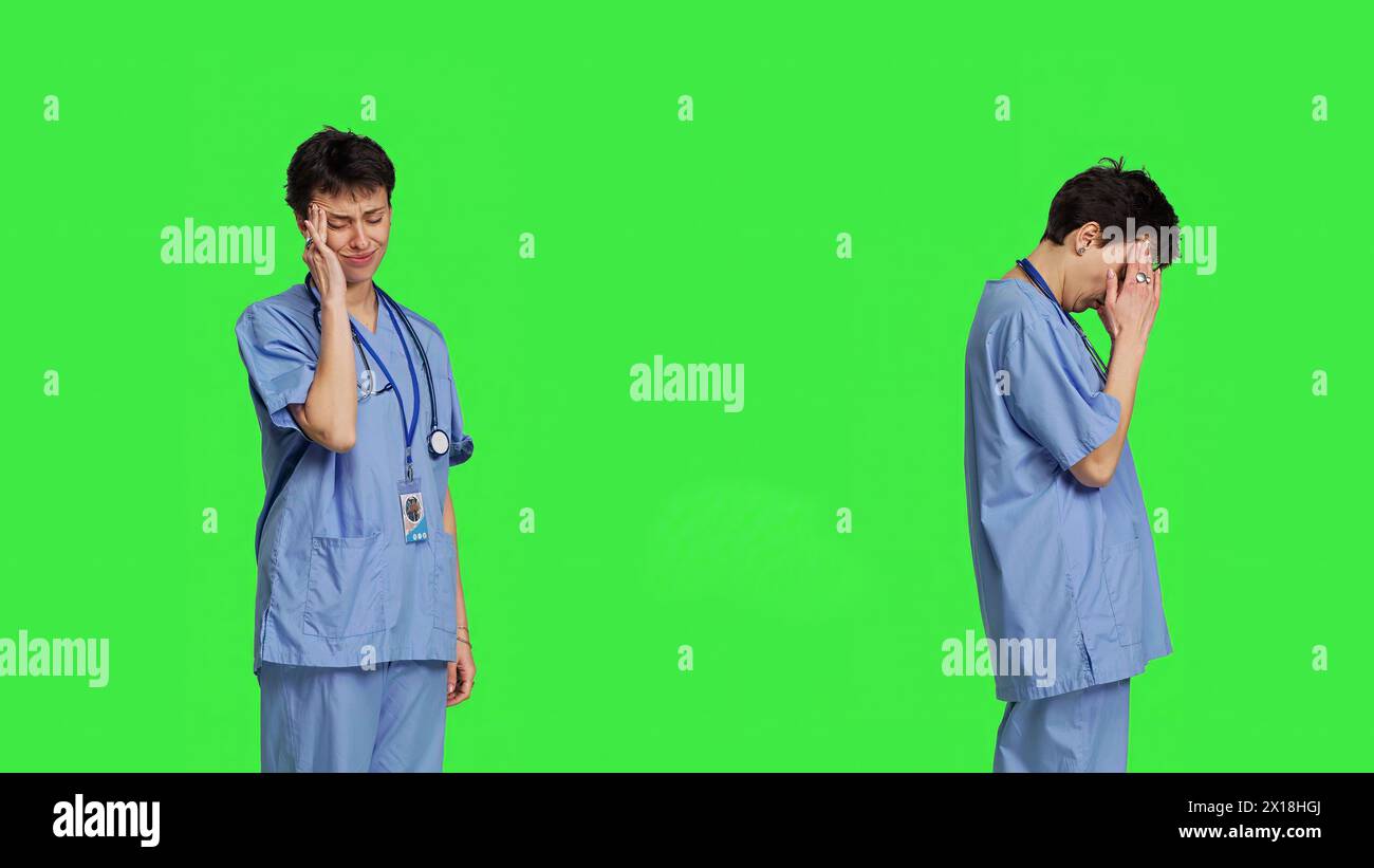 Unwell nurse suffering from a headache against greenscreen backdrop, wearing scrubs and feeling ...