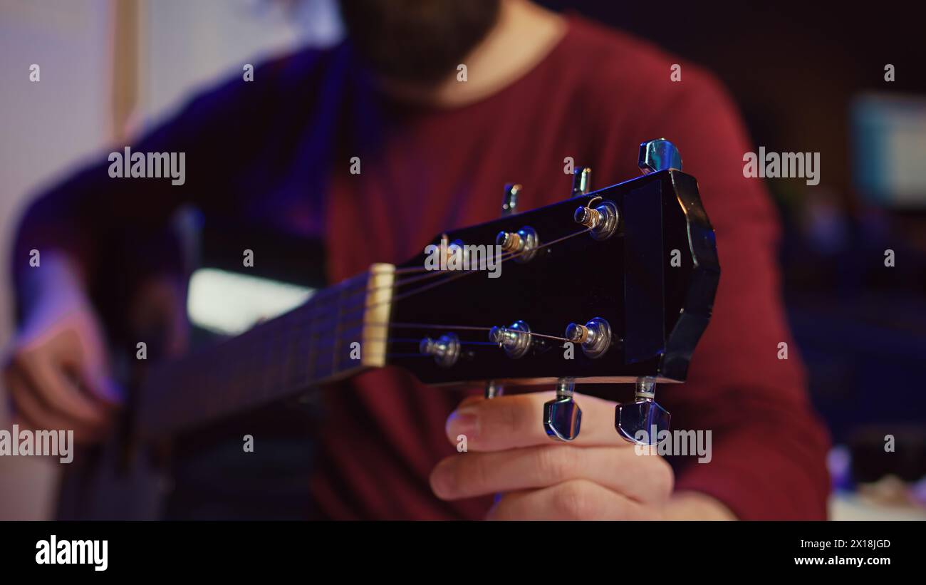 Musical performer tuning his guitar by twisting the knobs, preparing to ...