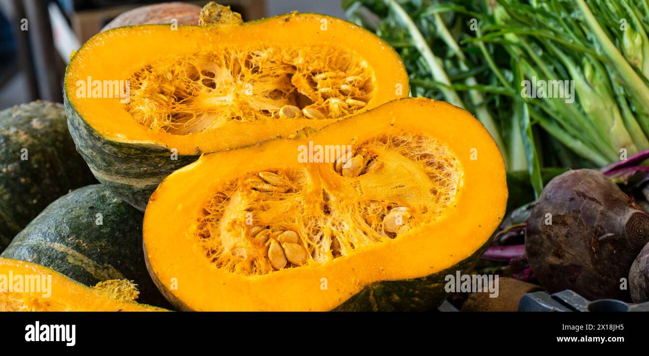 Orange squash cut in half with seeds, surrounded by leafy greens and ...