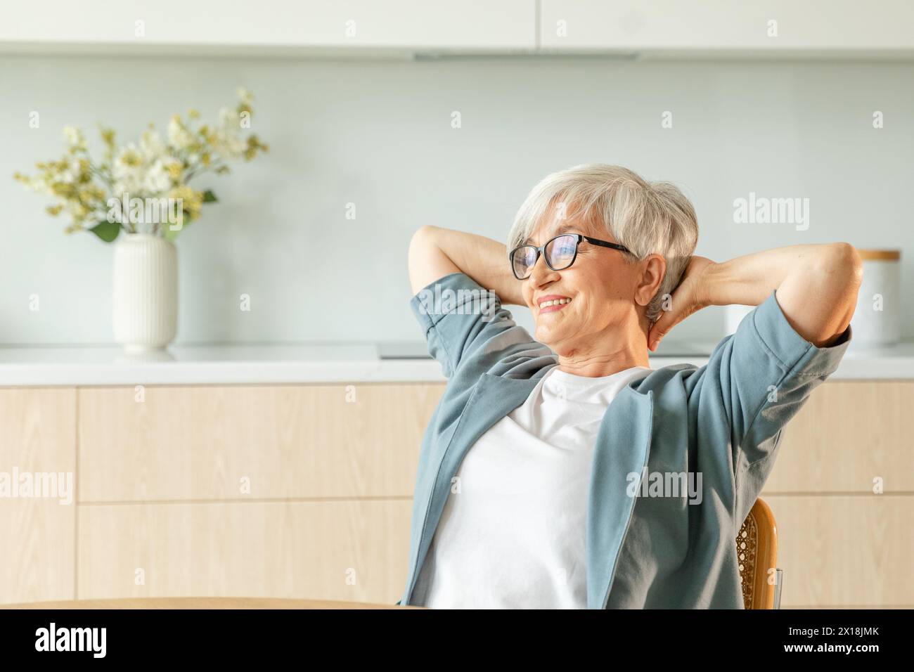 Senior old woman feeling relaxed stretching arms in kitchen at home. Smiling mature woman ...
