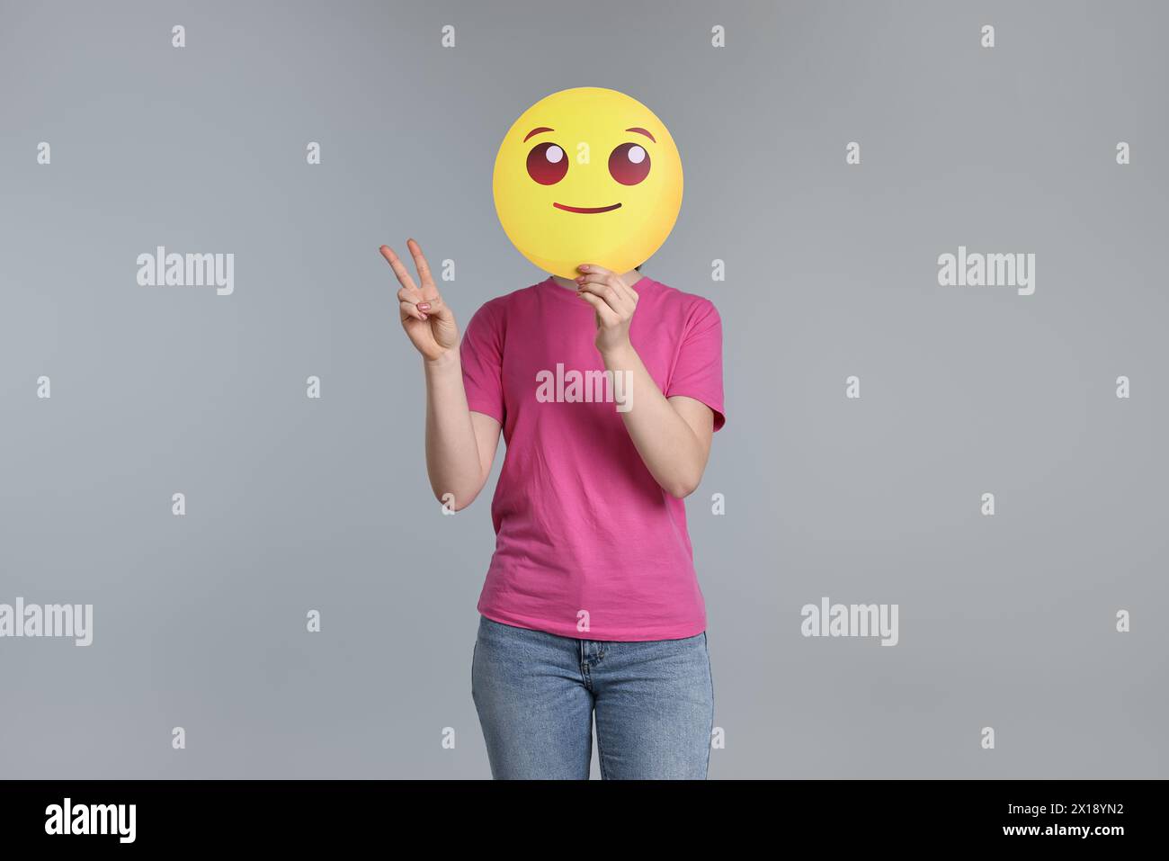 Woman covering face with smiling emoticon and showing peace sign on ...