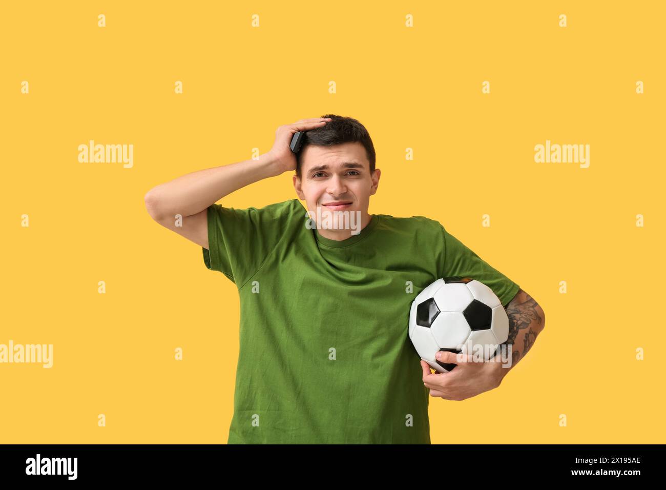 Sad man with soccer ball and TV remote control on yellow background ...