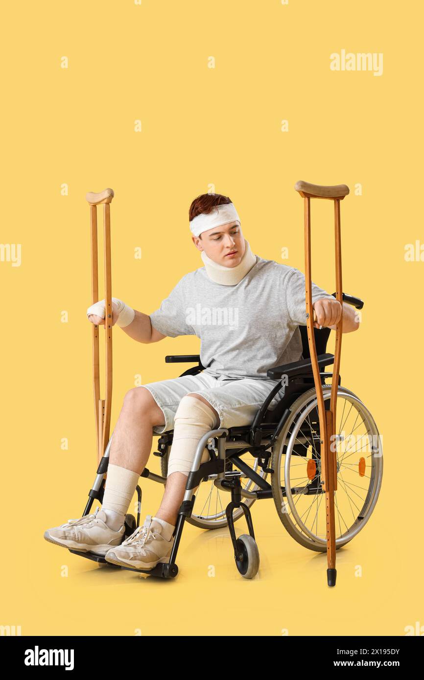 Injured young man after accident in wheelchair with crutches on yellow ...