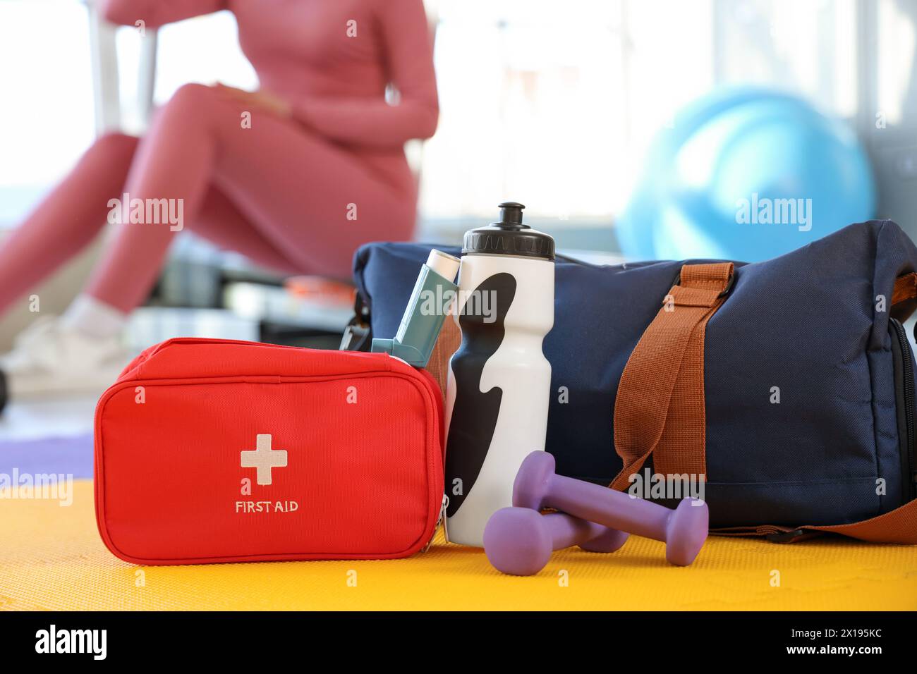 First aid kit with inhaler, dumbbells and sports bag in gym, closeup ...