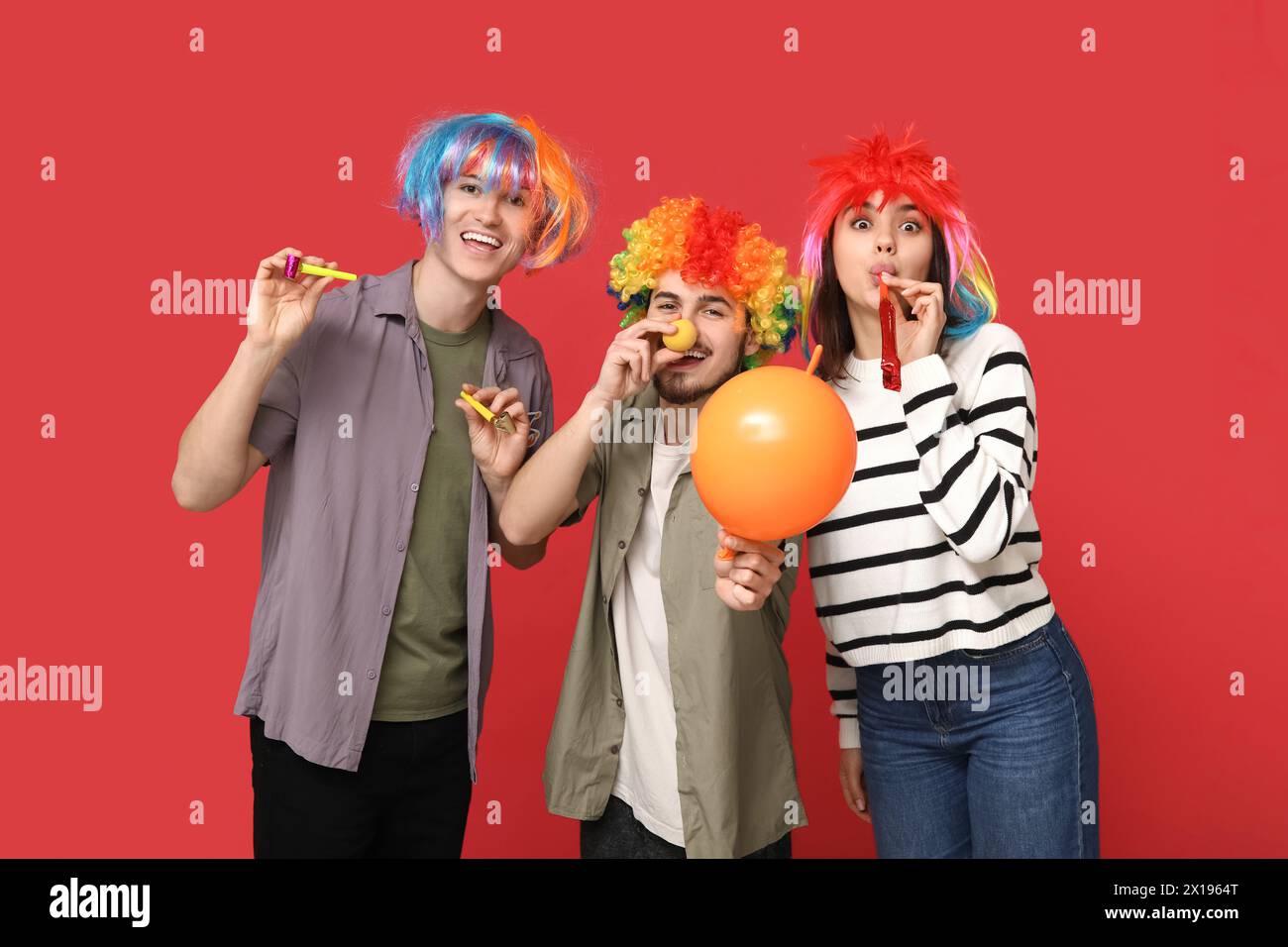 Young friends in funny disguise with party whistle and balloon on red ...