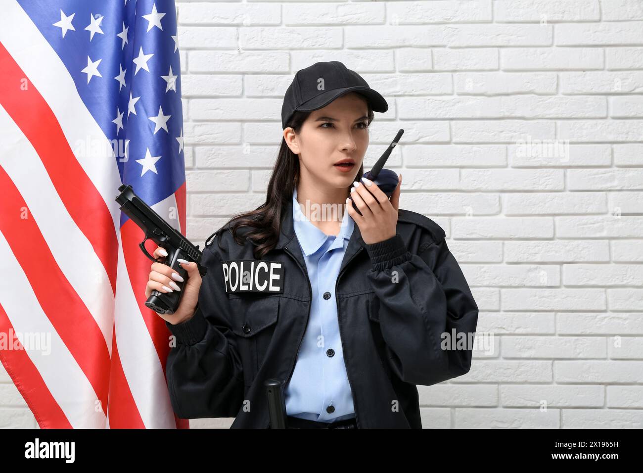 Female police officer with gun and walkie-talkie on white brick ...