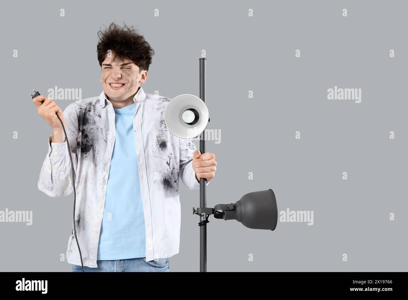 Electrocuted young man with burnt face and lamp on light background ...