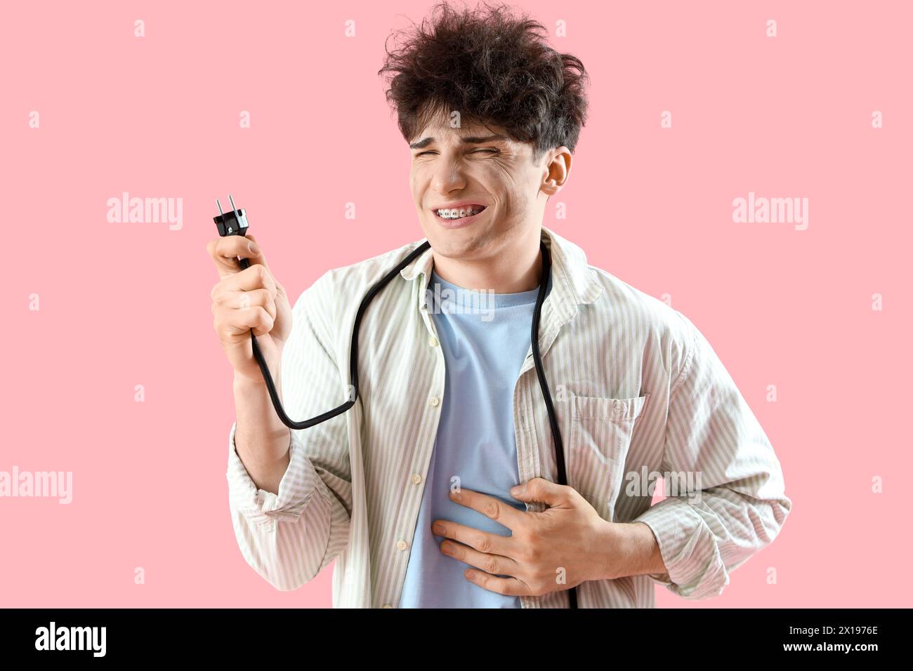 Electrocuted young man with burnt face and plug on pink background ...