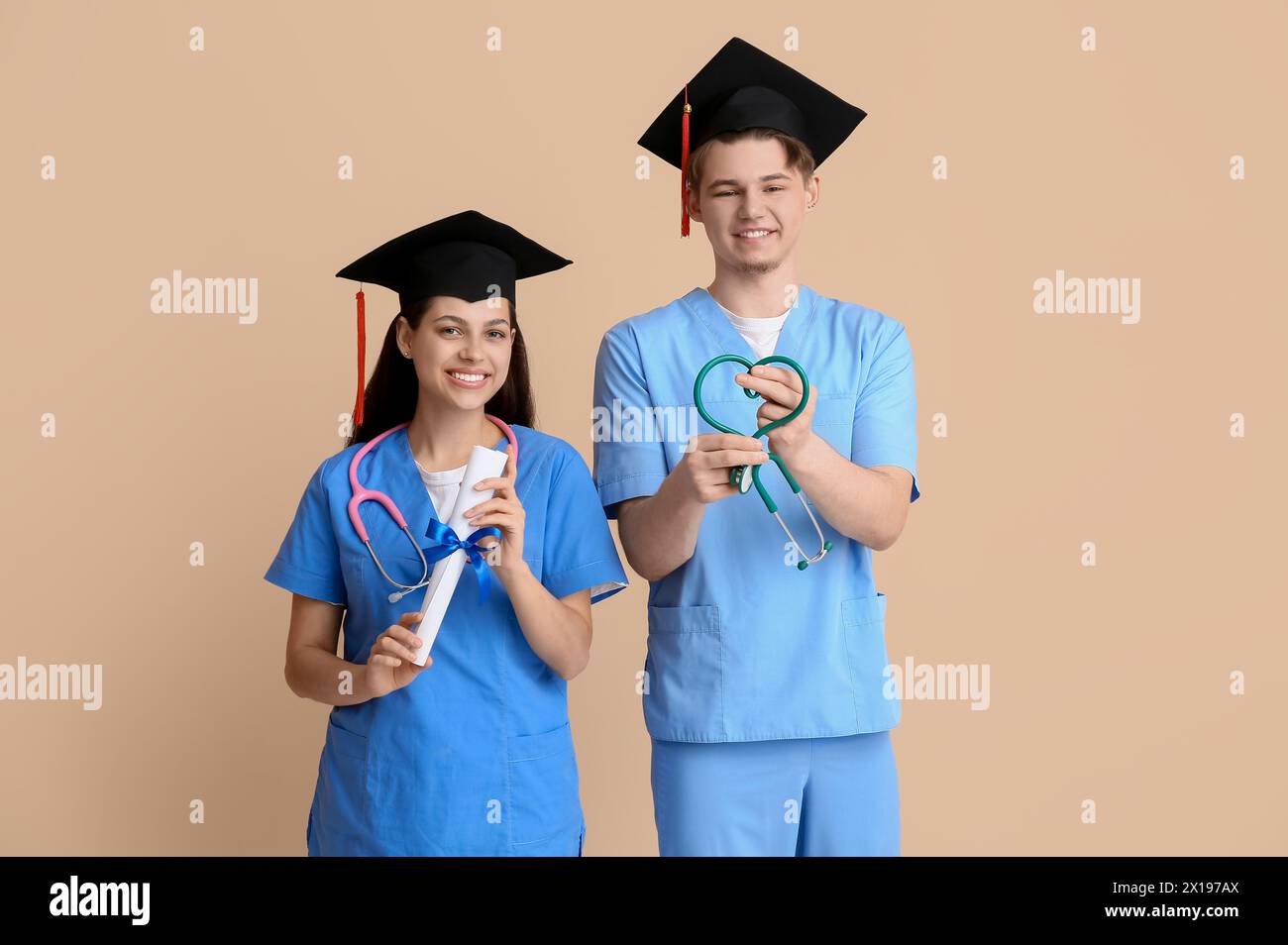 Happy medical graduate couple with diplomas and stethoscopes on beige ...