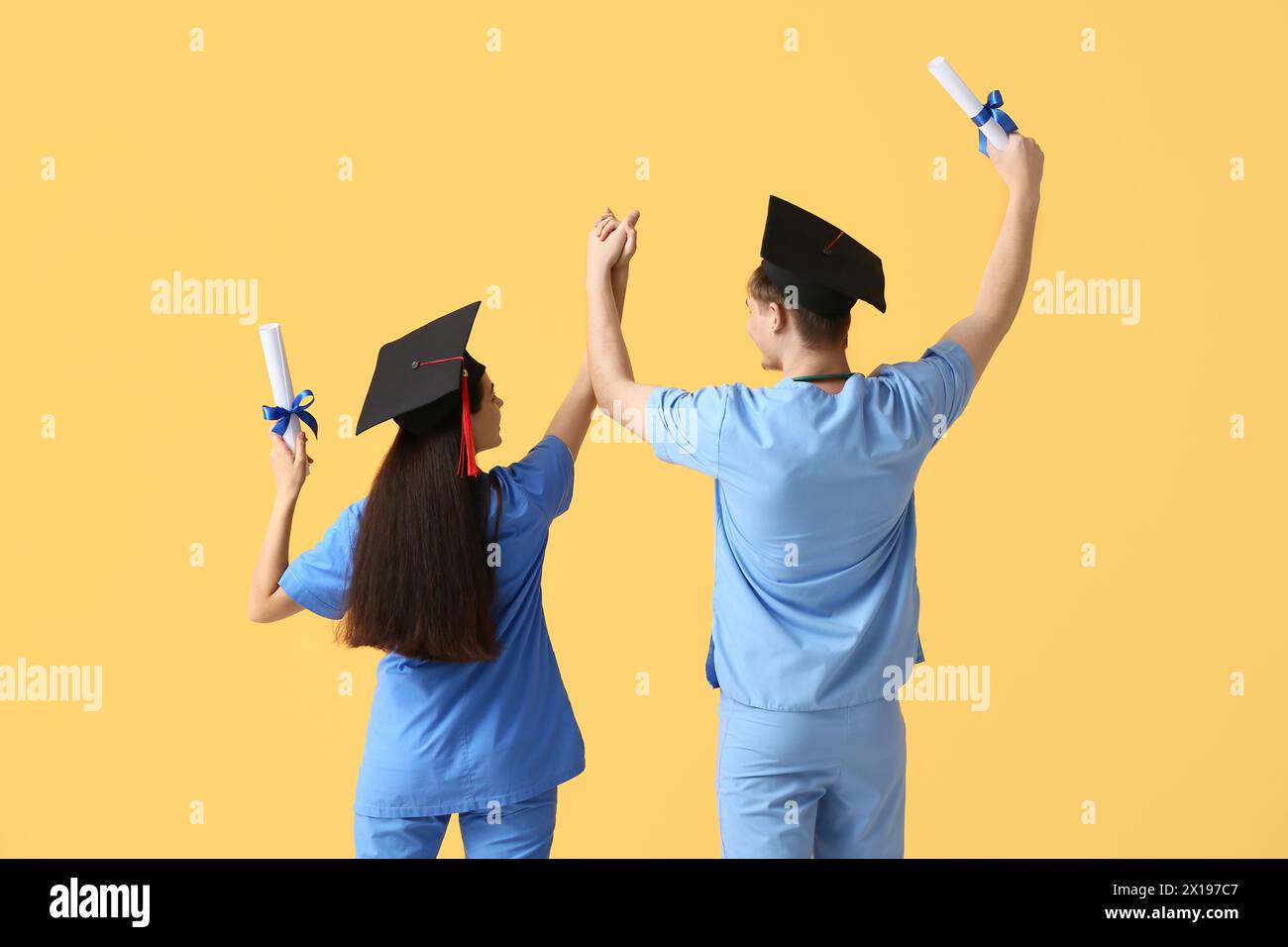 Medical graduate couple with diplomas on yellow background, back view ...