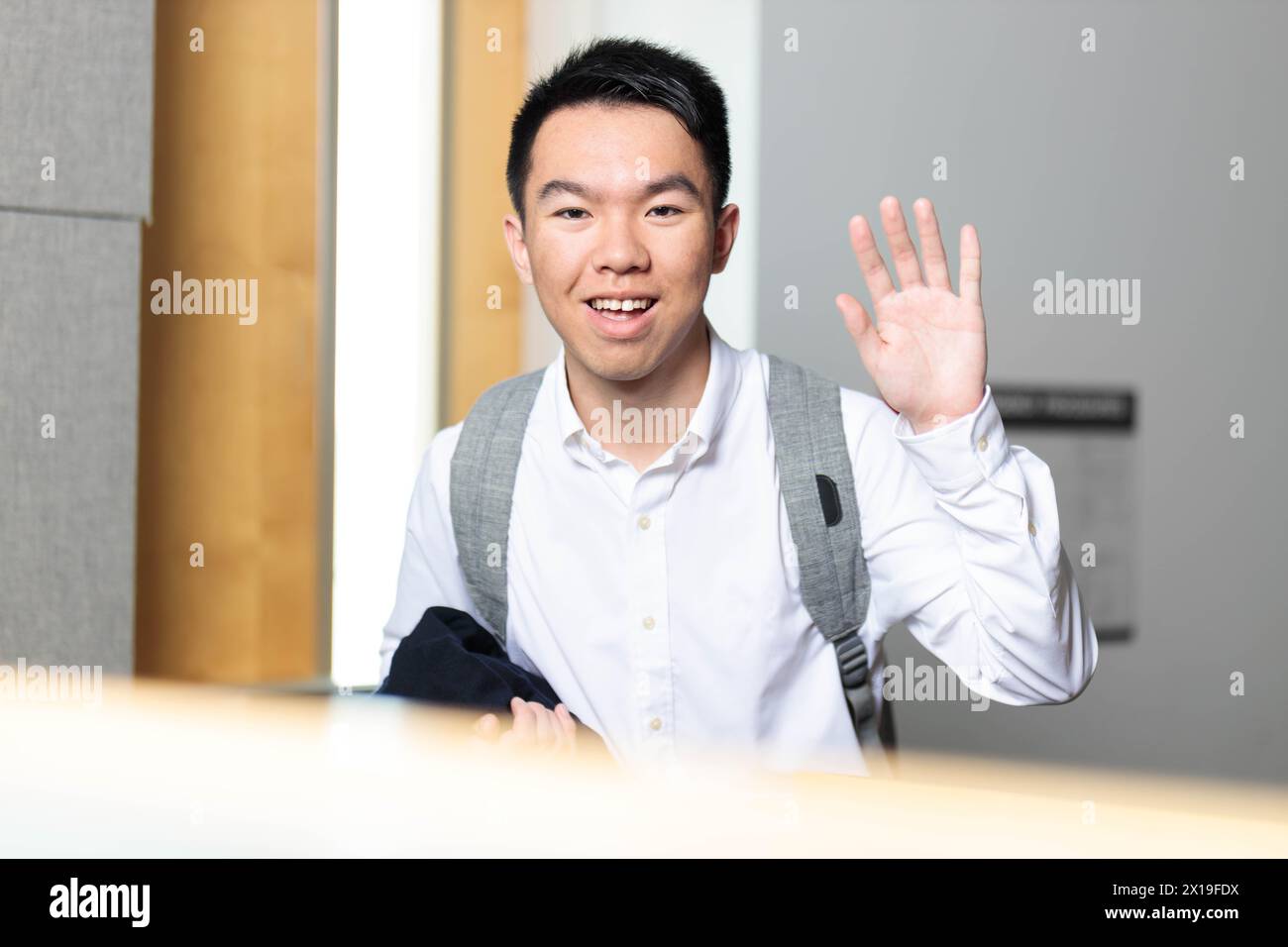 A male university business student with a backpack is waving his arm at ...