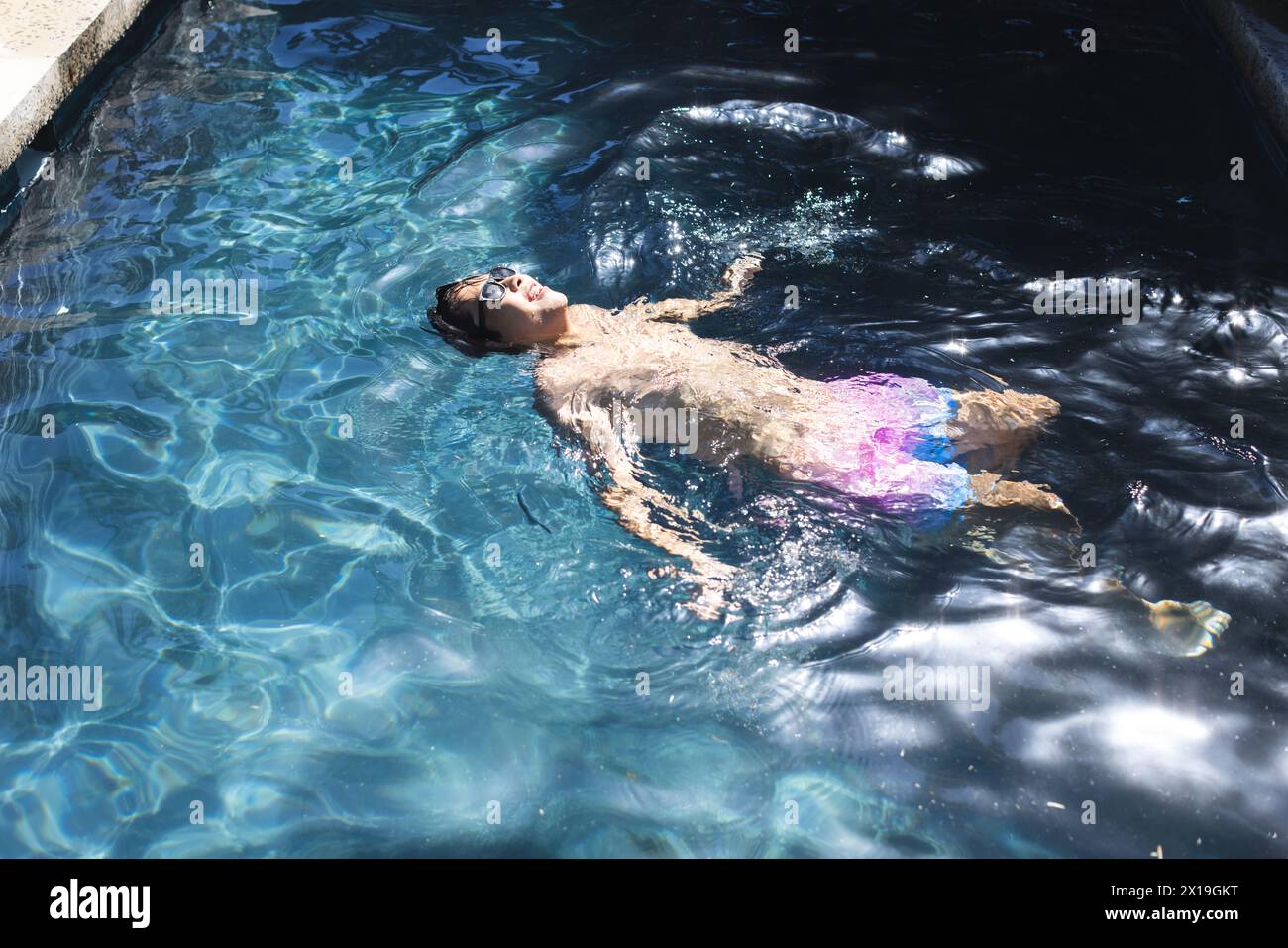 A teenage Asian boy floating in clear pool water outside at home ...