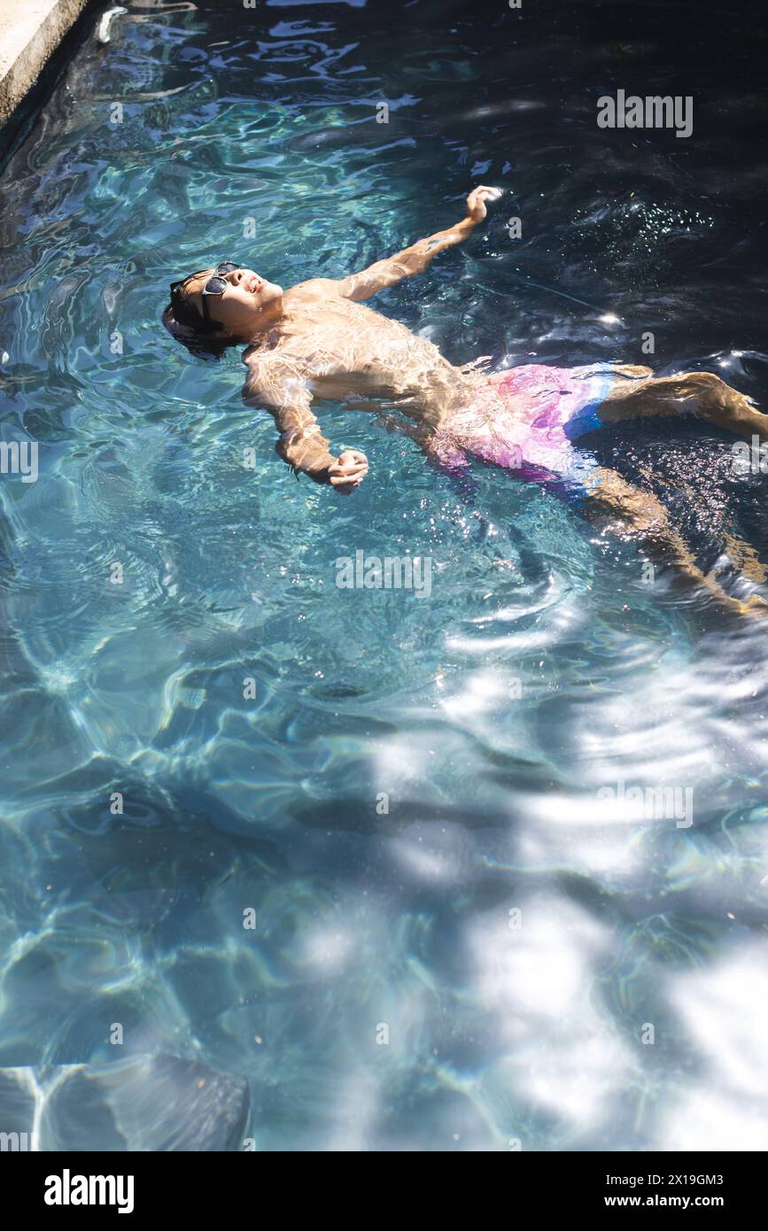 A teenage Asian boy floats in clear pool water outside at home ...
