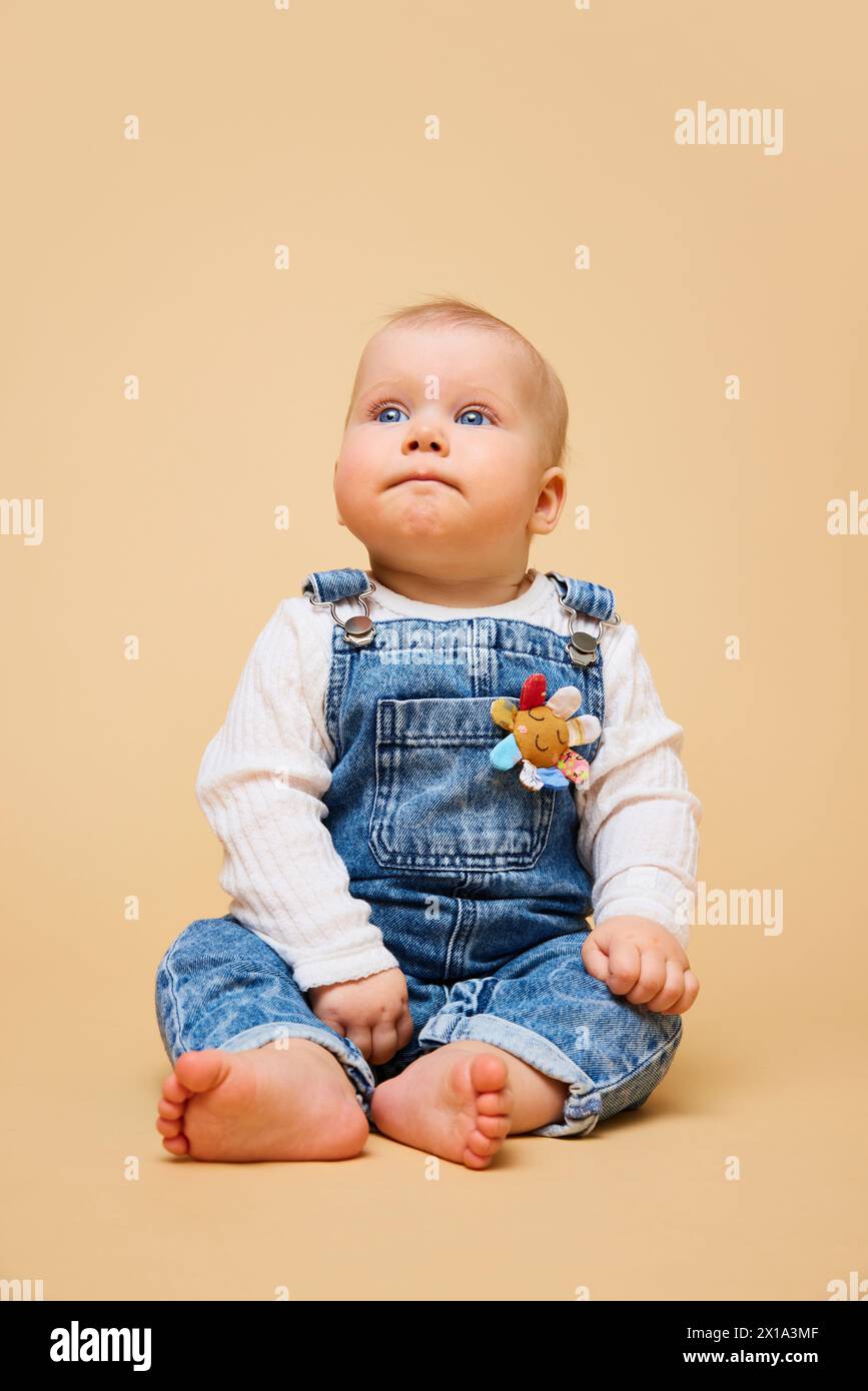 Baby with thoughtful expression looks upwards comfortably seated in ...