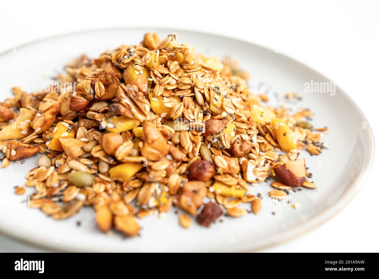 A bowl of granola with nuts and seeds on a white plate. The granola is ...
