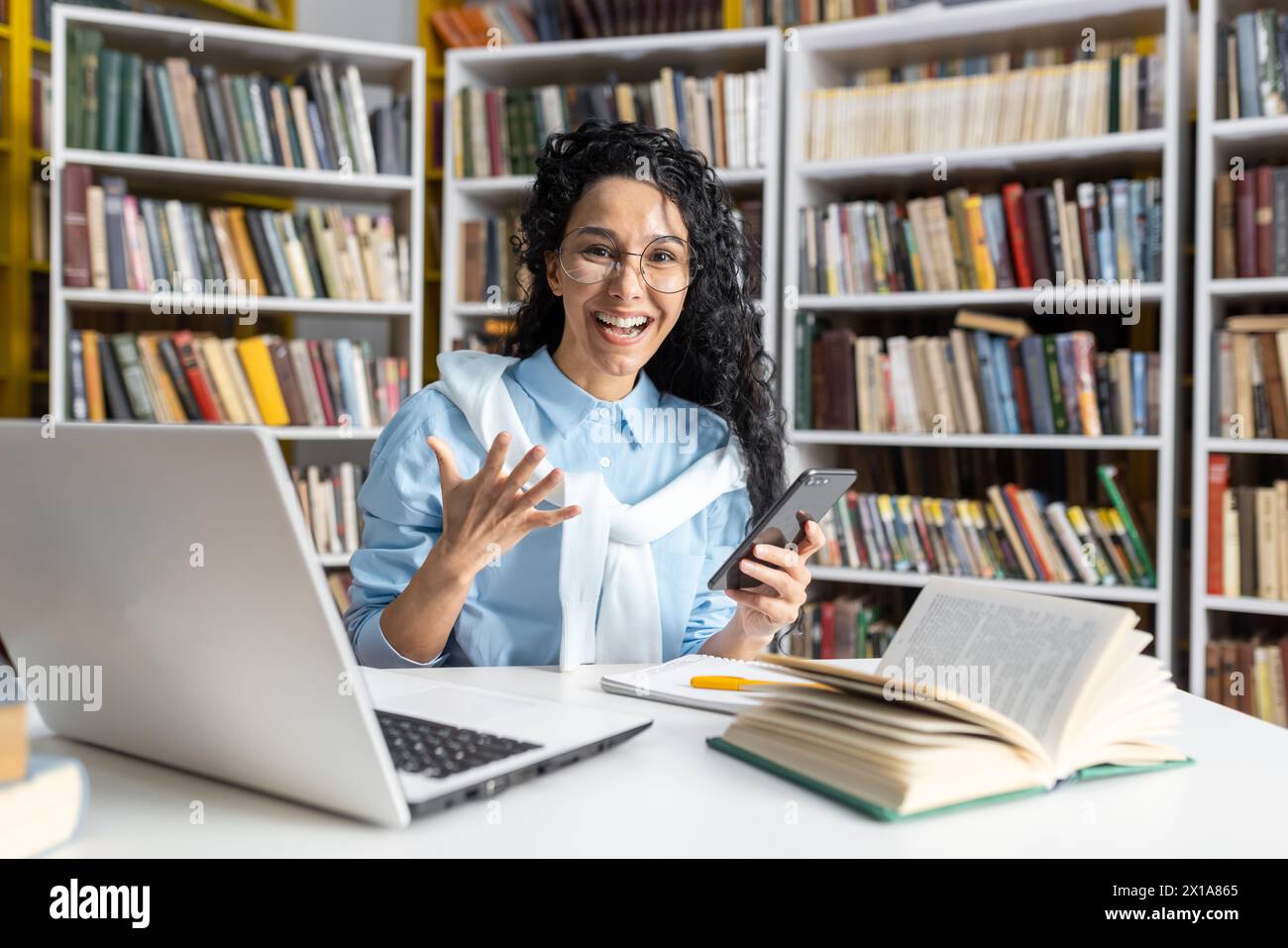 Cheerful young woman in glasses engages animatedly over a smartphone ...