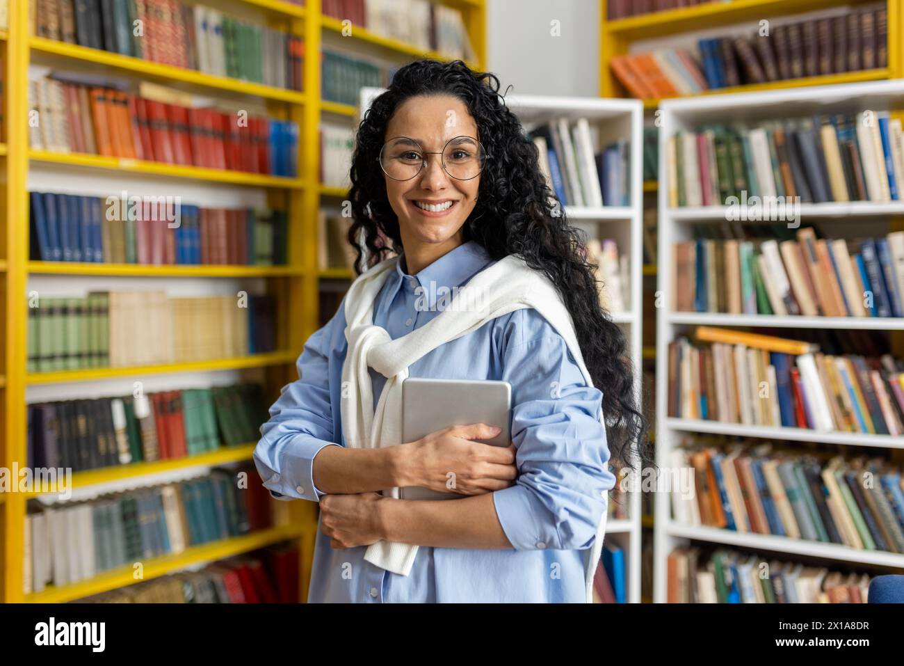 A cheerful, young woman stands confidently in a library, holding a ...