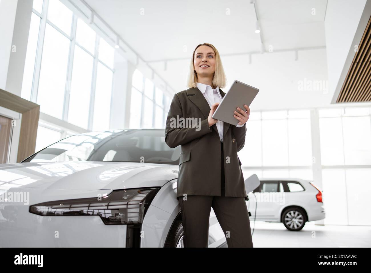 Professional smiling female car dealer posing at auto showroom holding ...