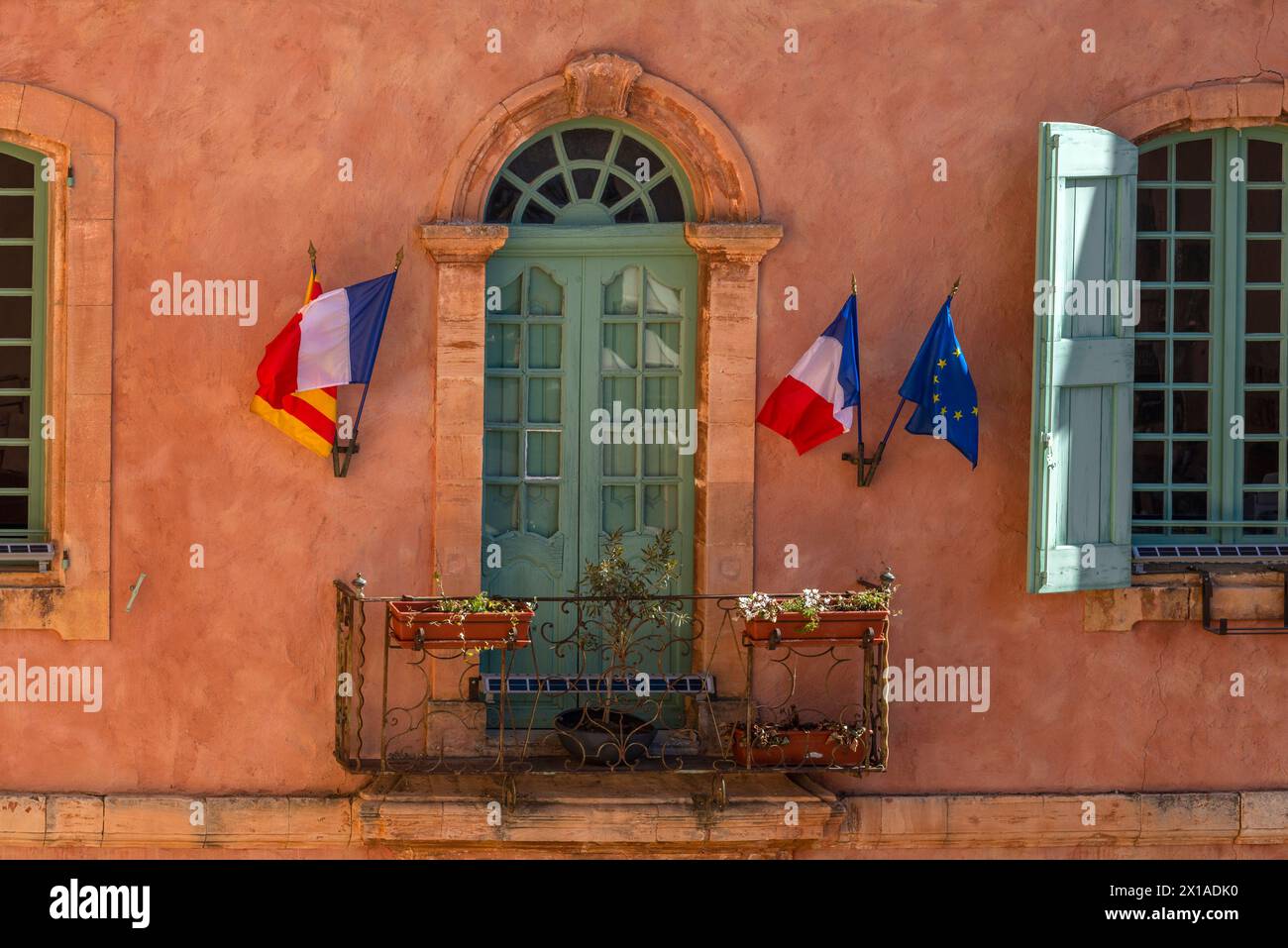 Two French flags adoring a Provencal balcony, with a green wooden door ...