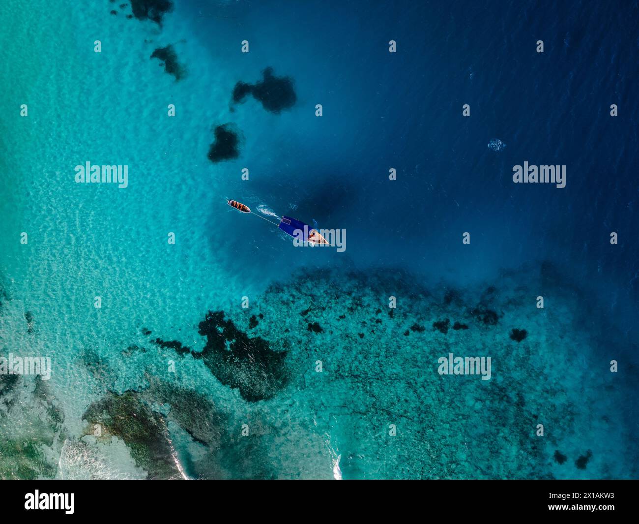 A boat towing a wooden boat behind over the beautiful blue Indian Ocean ...