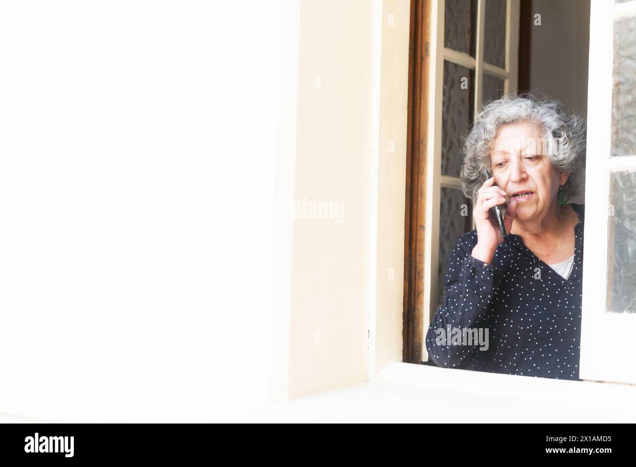 Seventy-year-old woman talking on her smart phone from the window of ...