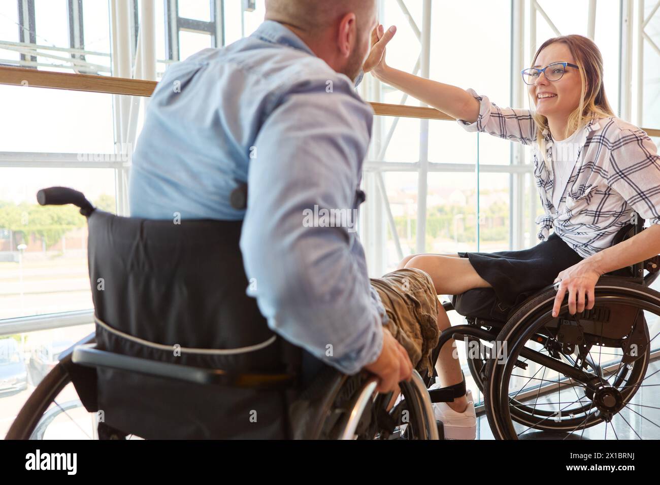 A woman and man, both using wheelchairs, share a joyful high-five in a ...