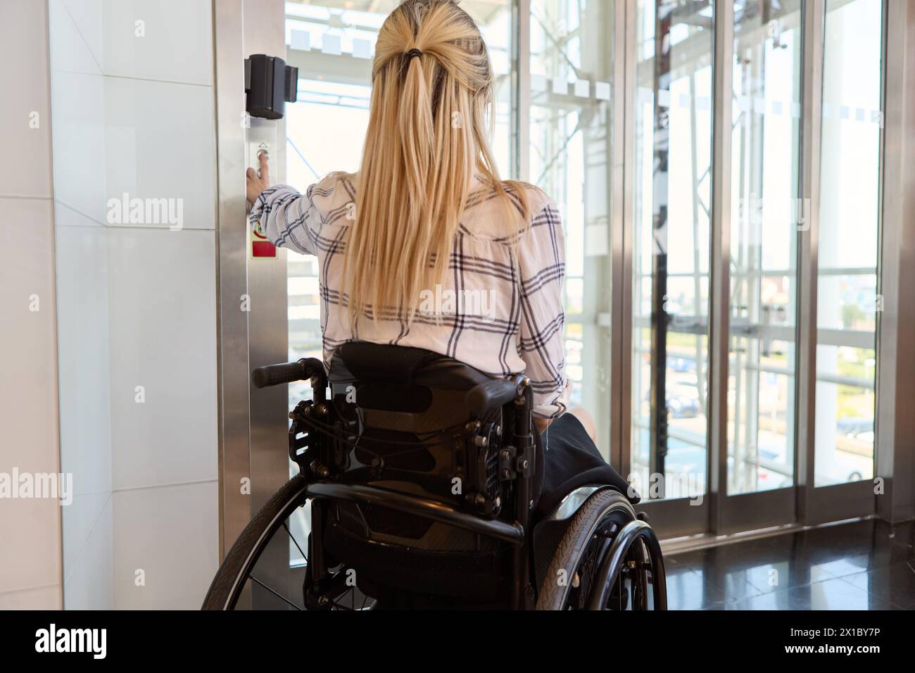 A person using a wheelchair reaches for an elevator button ...